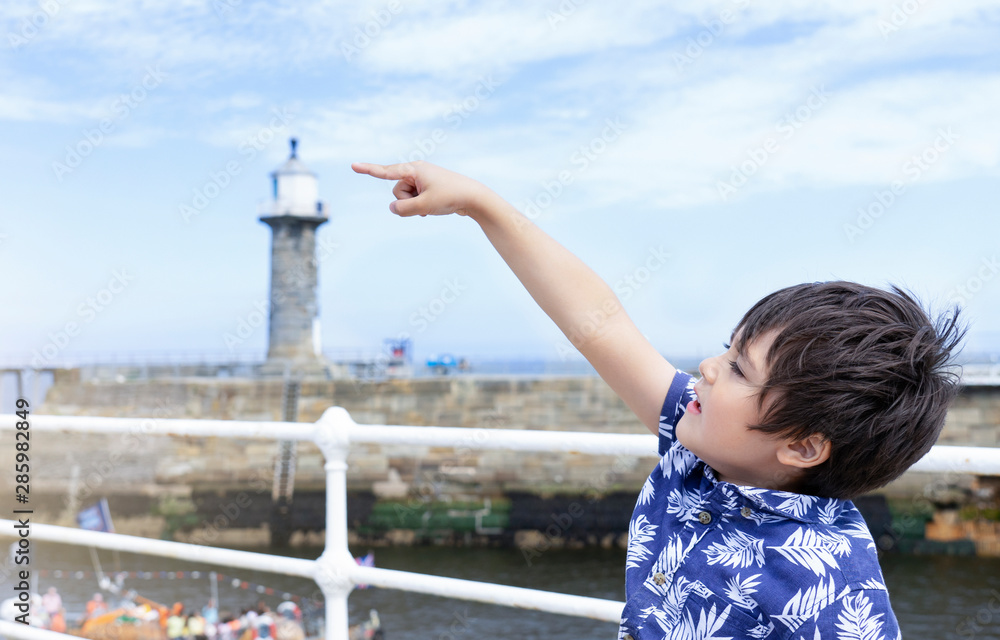 Portrait of cute little boy pointing finger up to sky, Side view active ...