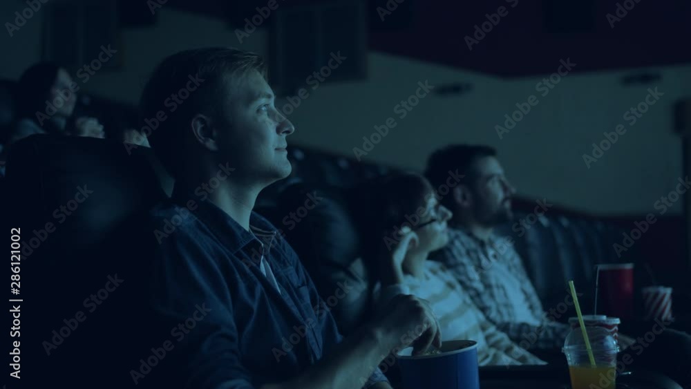 Crowd of cheerful young people watching film in cinema eating popcorn ...