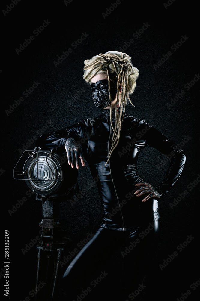 Young cyborg woman in leather suit and a gas mask leaning on a ...