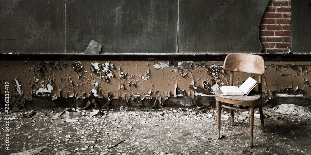 Old chair in front of a chipped chalkboard of the abandoned St ...