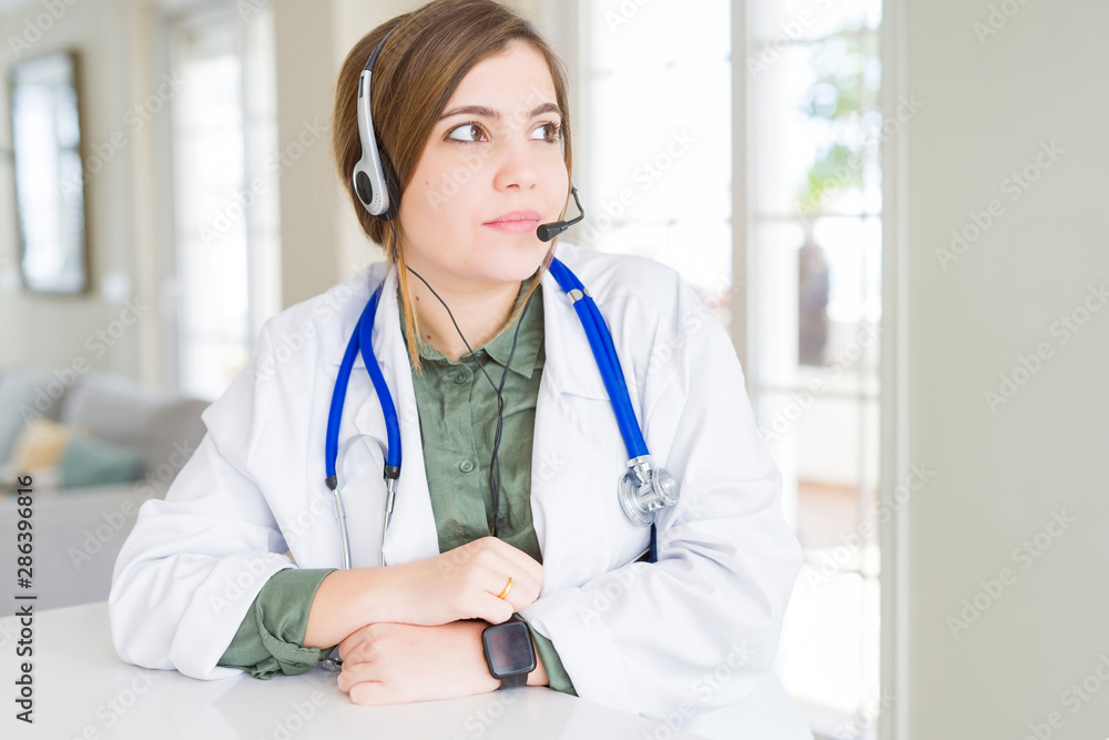 Beautiful young doctor woman wearing headset looking to side, relax ...