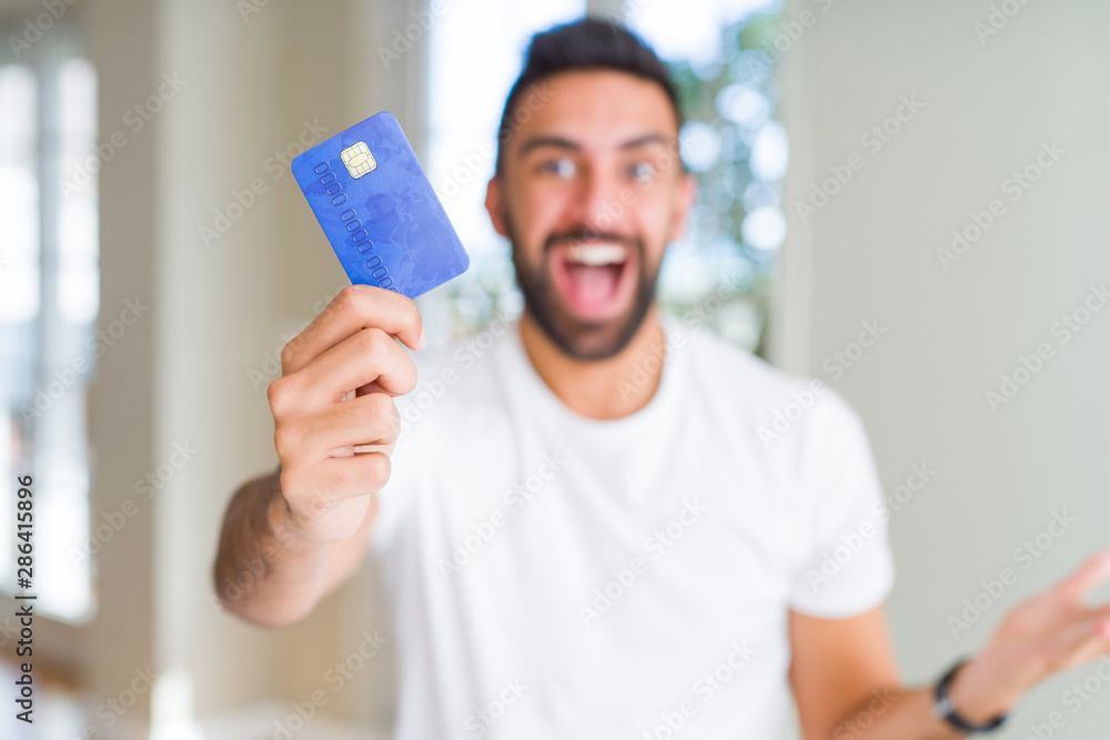 Handsome hispanic man holding credit card very happy and excited ...