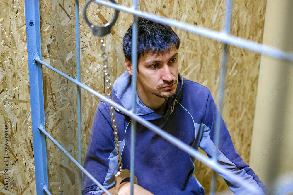 A white man is sitting in solitary confinement behind bars in a prison ...