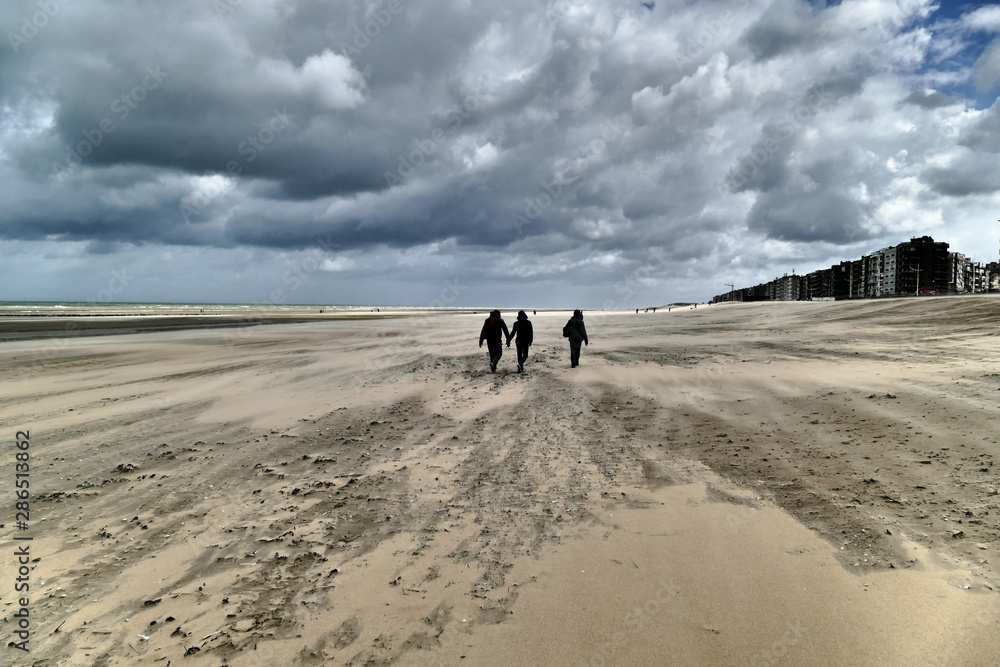 People walking on the beach with impressive sky and clouds during a ...