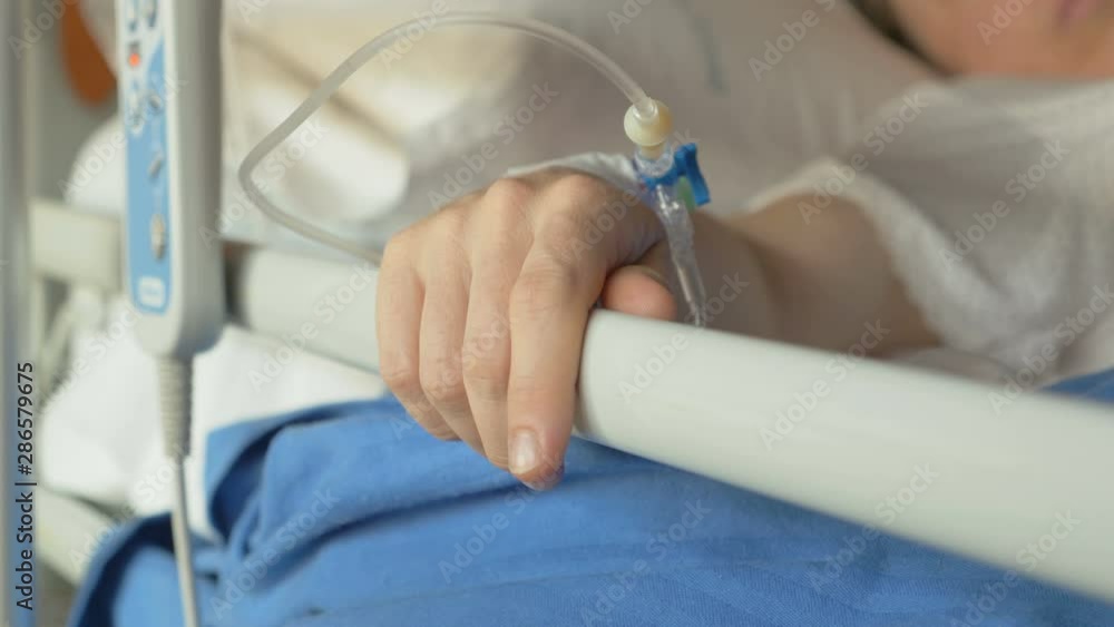 Patient in the ward with a medical IV drip and intravenous needle in ...