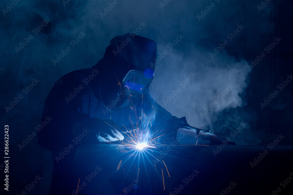 Professional welder and mask welding metal pipe on the industrial table ...
