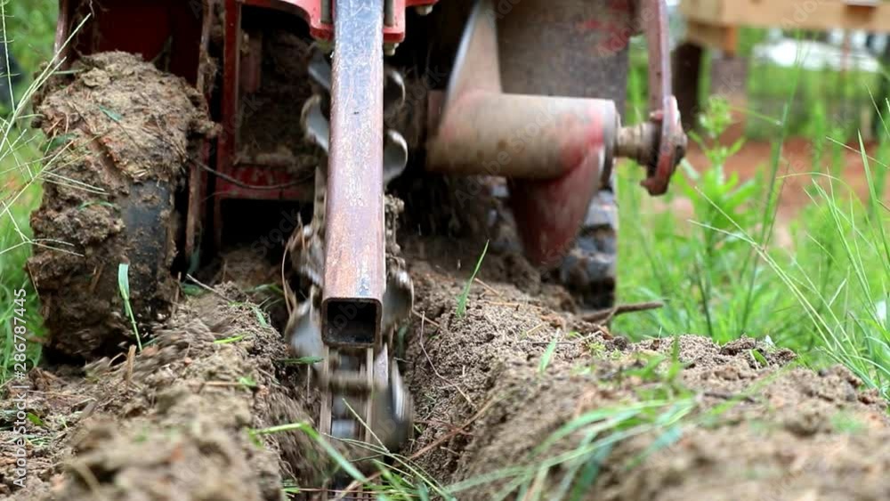 Close up view of utility trench being cut by machine. BOOM UP to view ...