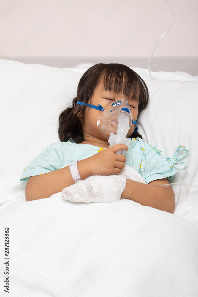 Little Asian girl is sick in a bed with an oxygen mask in hospital ...