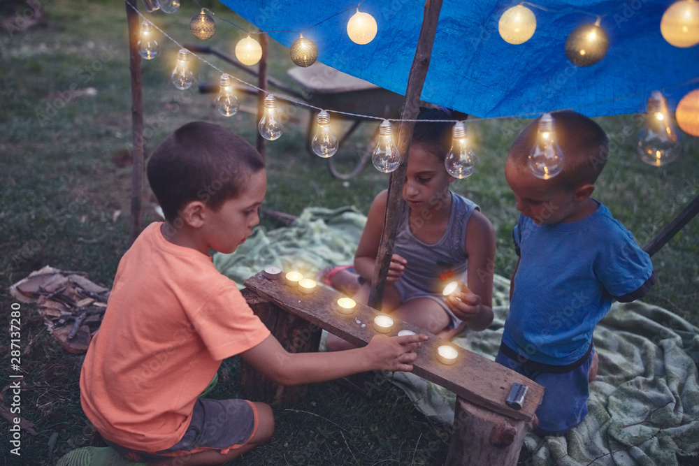 Kids making a small tent with candles and lampions in the backyard ...