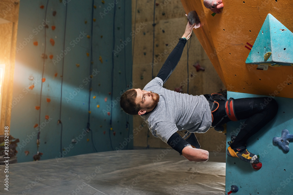 Powerful handsome boulderer without forearm, training at climbing gym ...