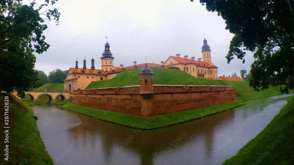 An ancient feudal castle surrounded by a water moat. It is raining ...