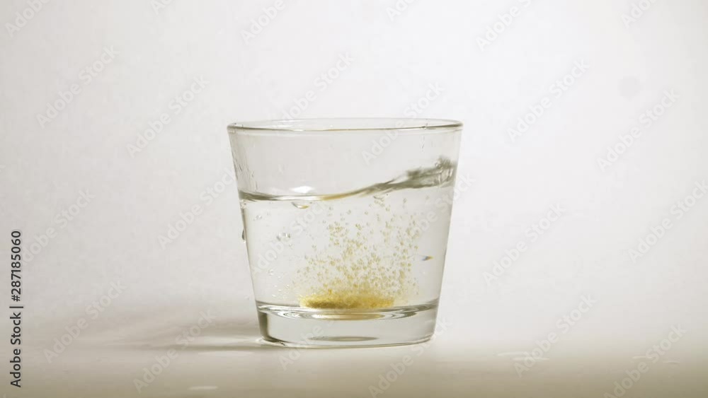 White effervescent tablet falls into a glass of water. Pills dissolves ...