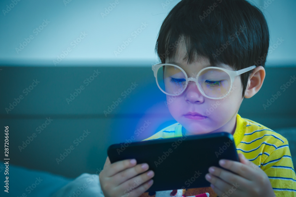 Cute little child watching cartoon on smartphone in the dark room ...