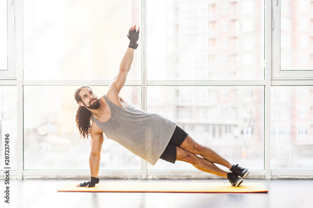 Young adult sporty muscular man with curly long hair practicing yoga ...