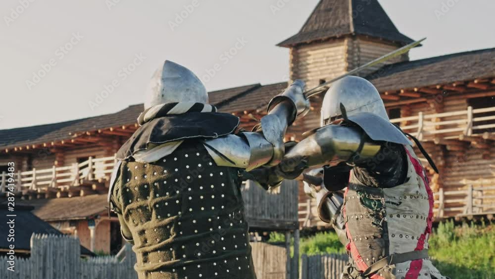 Battle of two knights in armor near wooden fortress. Metal armor ...