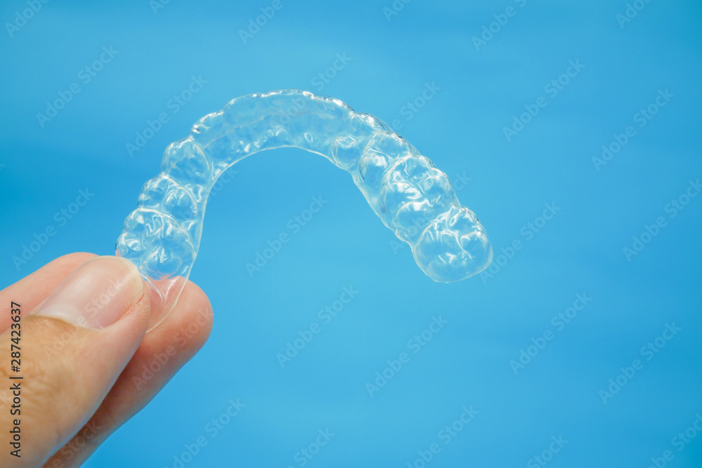 hand holding clear plastic retainer teeth that isolated on blue sky ...