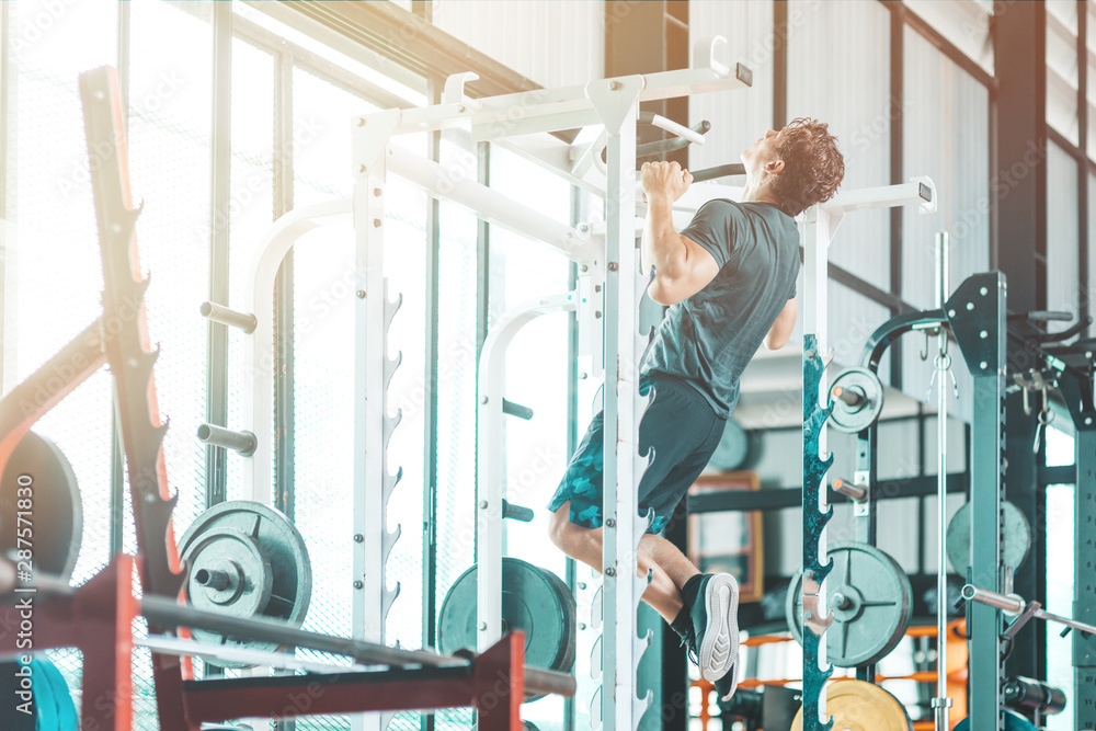 Full-length portrait of muscular man doing abs workout, pull-ups while ...