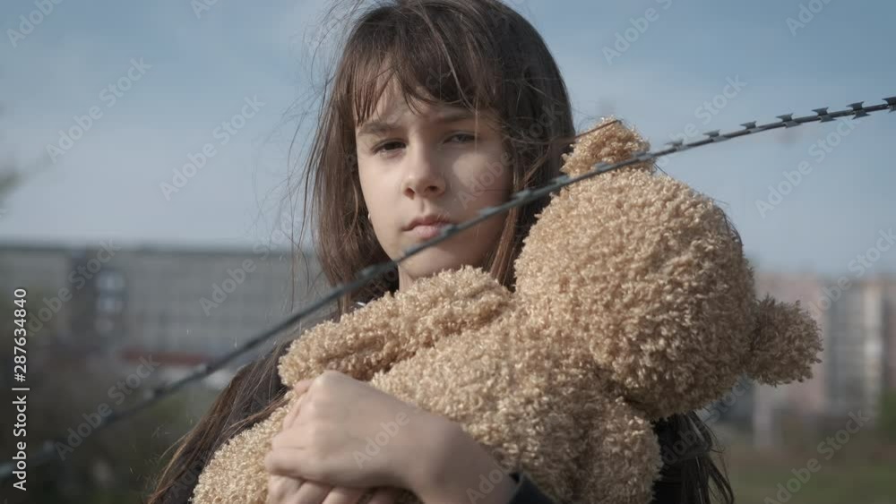 Homeless child with a teddy bear. Sad orphan girl with a bear behind a ...