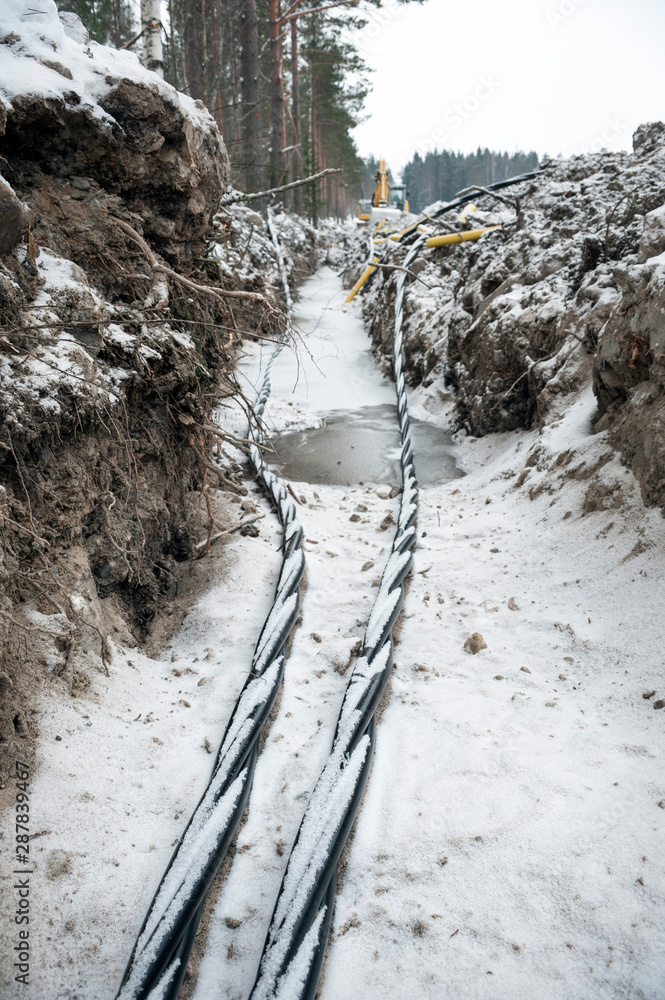 Laying a fiber optic and electricity cables in the frozen ground ...