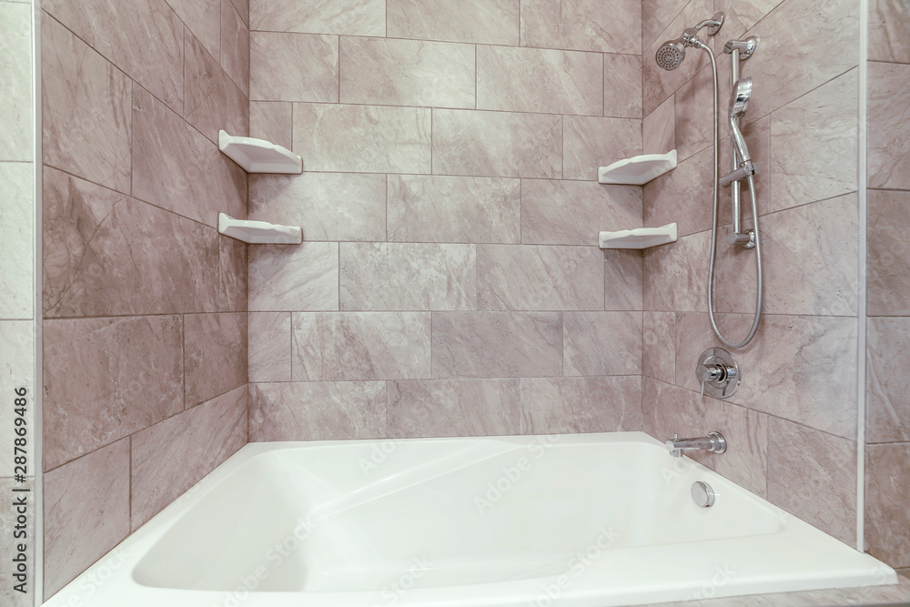 Square bathtub and stainless steel shower against gray and white tile ...