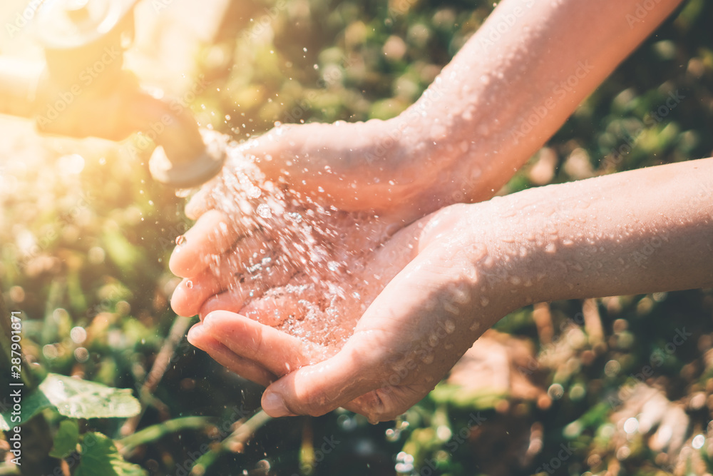 Water from tap to woman hand in nature green park and sunset sky with ...