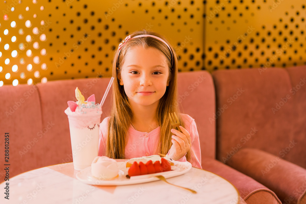Cute beautiful girl in a cafe eating a cake and a unicorn cocktail ...