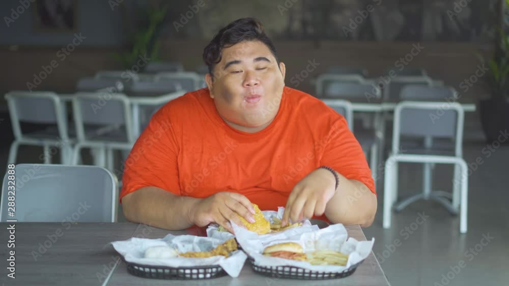 Greedy obese man eating big hamburger and french fries on the table in ...