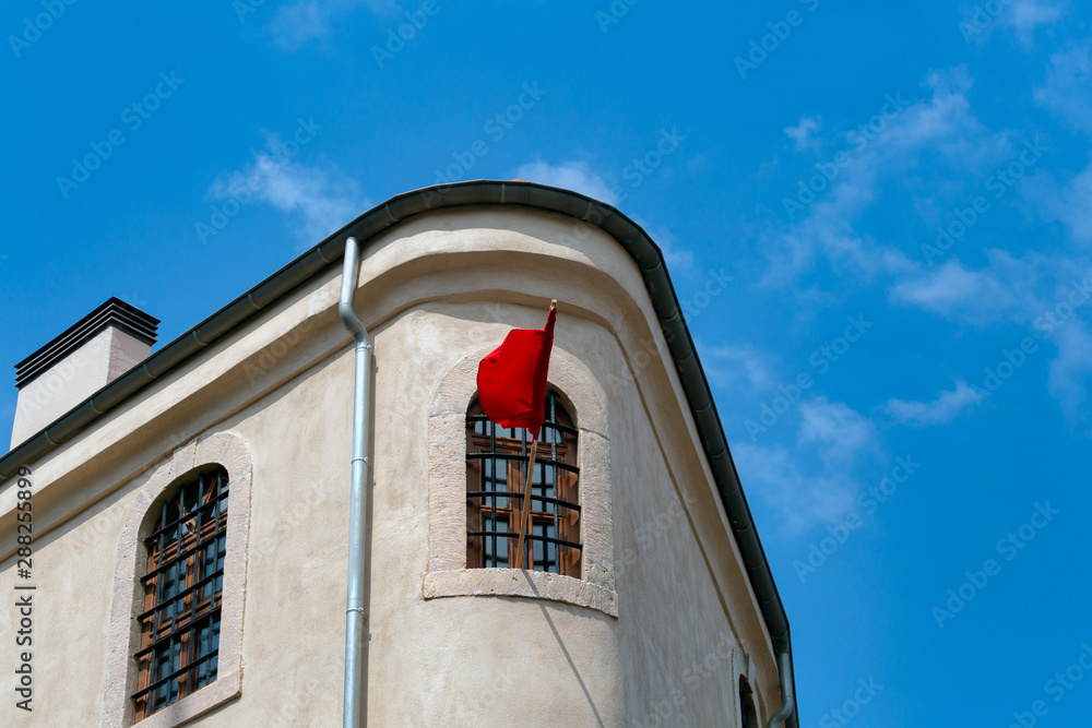 Red flag hanged on the round corner of an old concrete building with ...