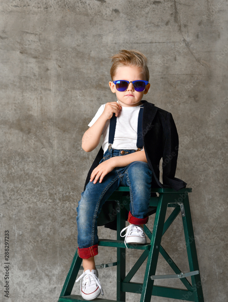 Cute stylish boy sitting on chair near concrete wall Stock Photo ...