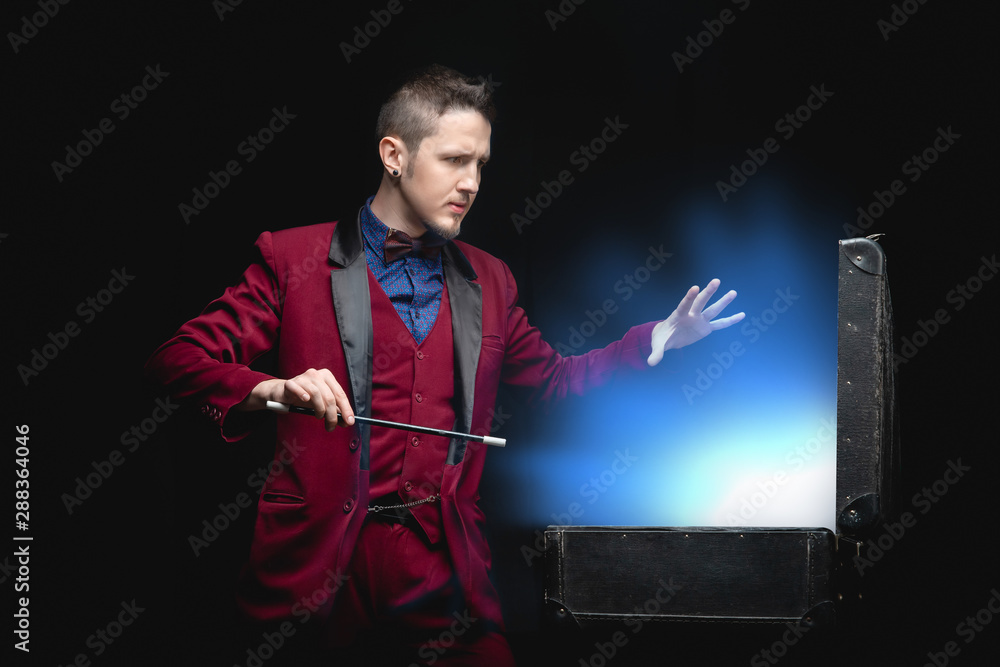 Magician man with magic wand shows disappearance in suitcase blue glow ...