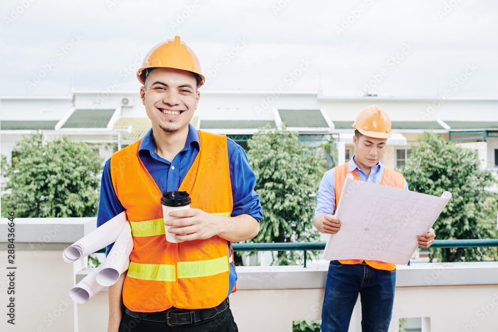 Smiling civil engineer standing outdoors with many blueprints scrolls ...
