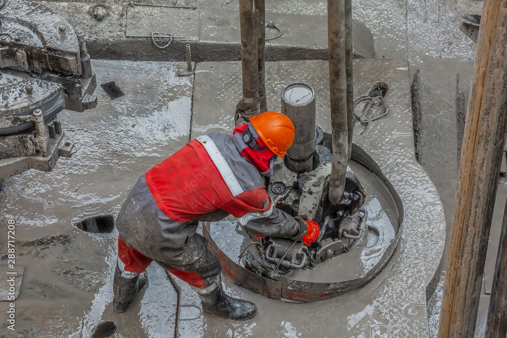 Work driller in red uniform, in helmet and goggles. He with the help of ...