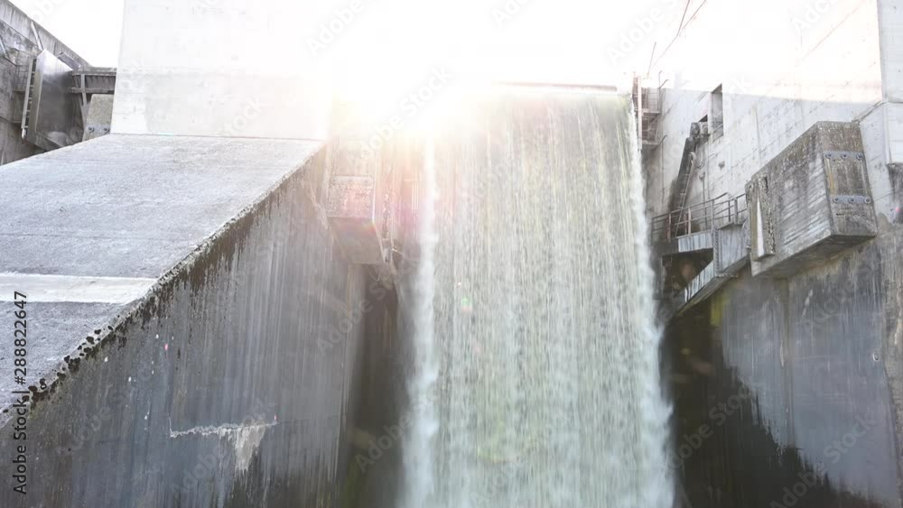 Waterfall of a hydroelectric plant in the late afternoon. Sun shines ...