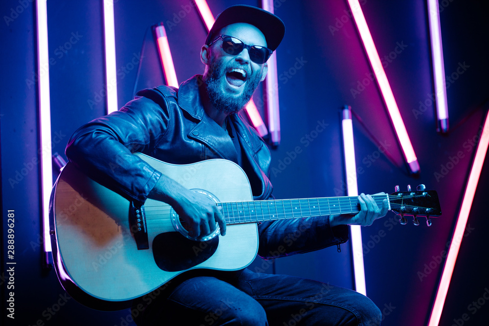 Singer and guitar player singing on a stage with neon lights. He is a ...