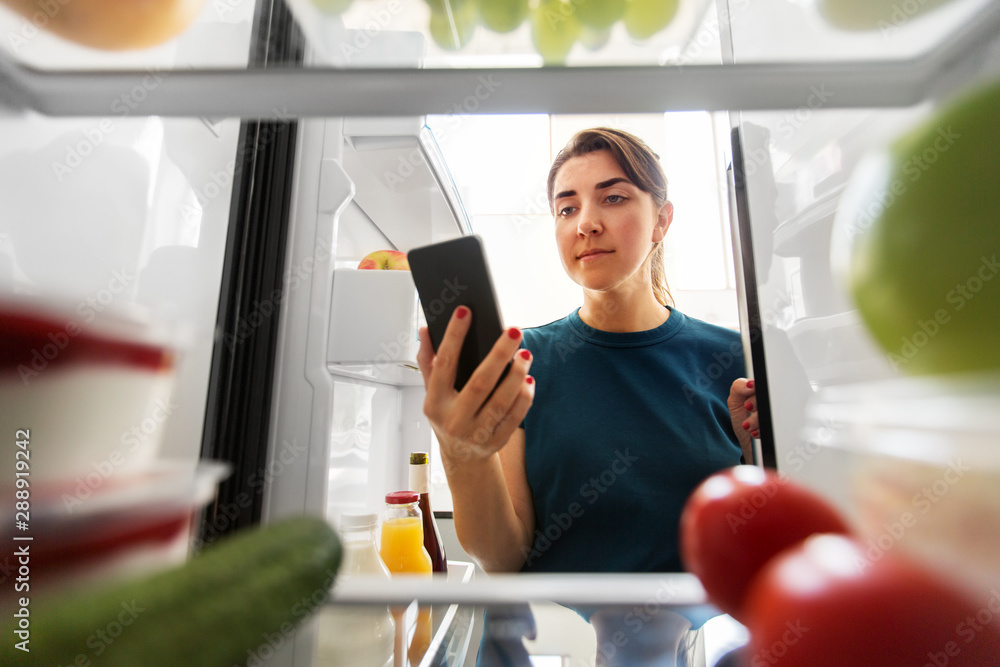 healthy eating and diet concept - woman at fridge with smartphone making list of necessary food ...