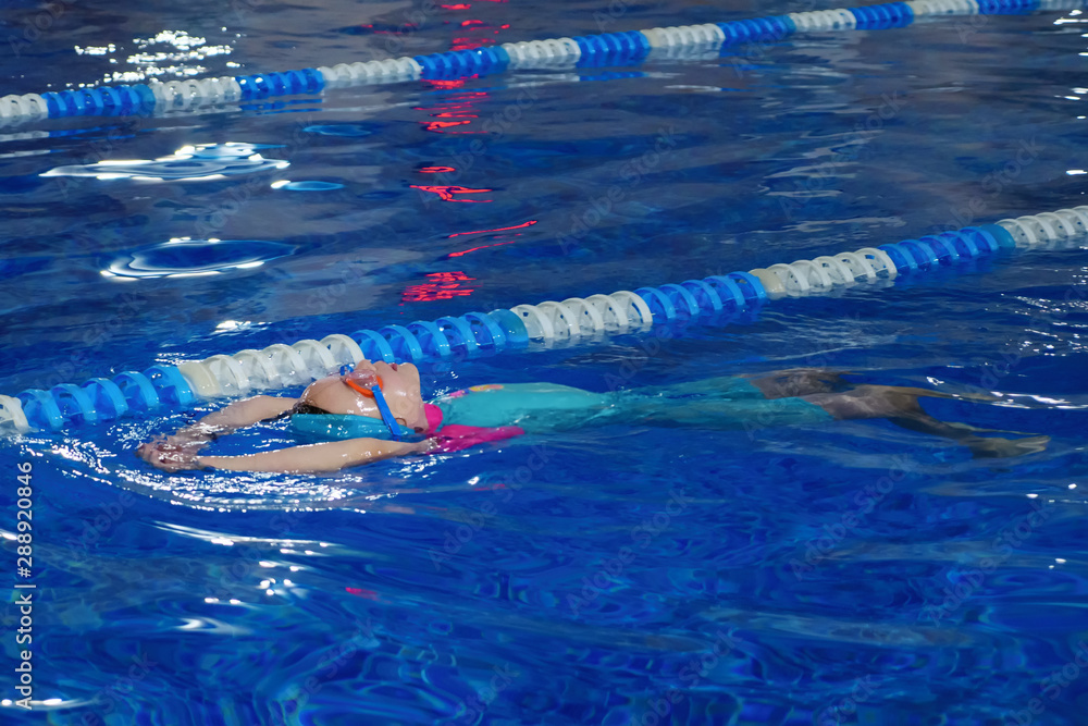 girl in goggles, swimsuit and cap is training swimming in pool. Child ...