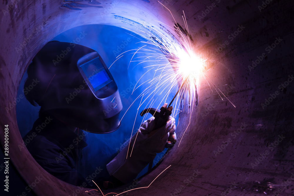 Welding of large pipes by industrial workers wearing safety equipment ...