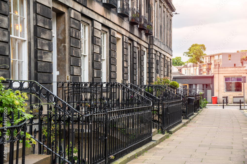 Fotka „Old stone terraced houses with metal fences along a street at ...