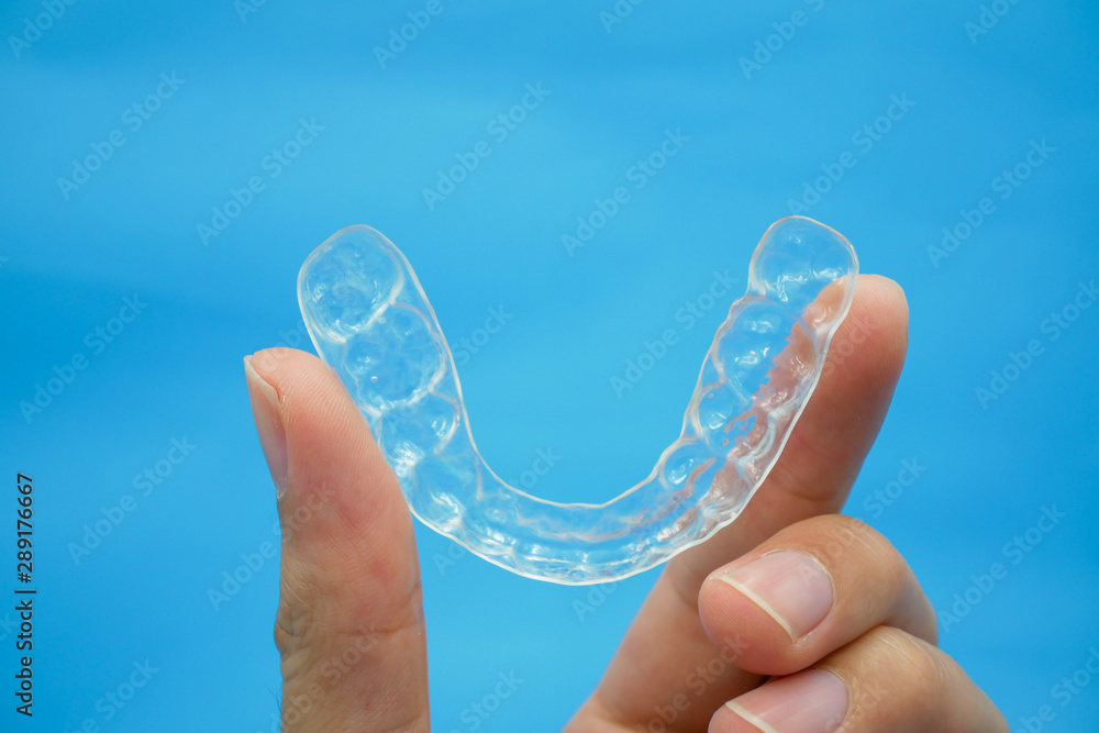 hand holding clear plastic retainer teeth that isolated on blue sky ...