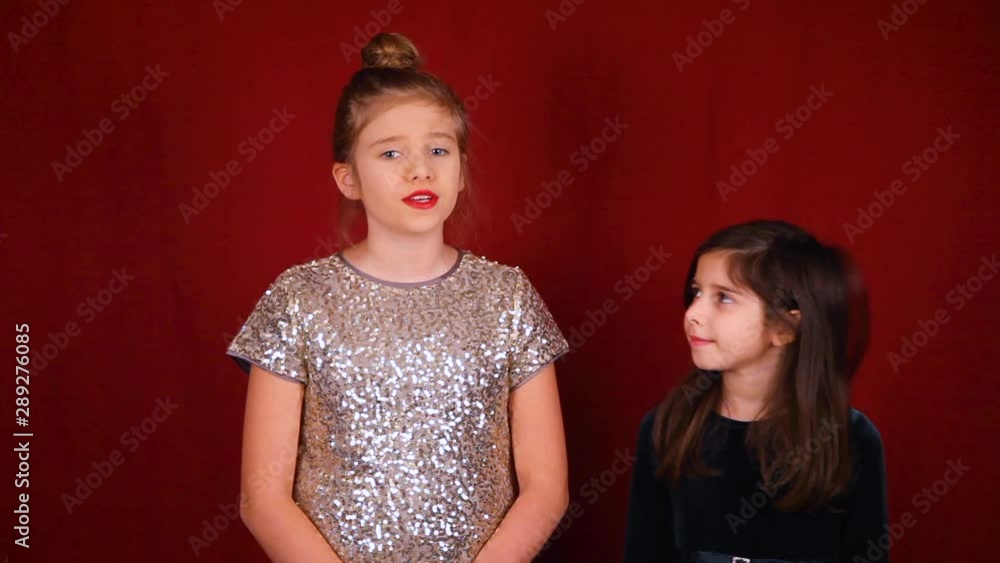 Two girls sing duet in front of red backdrop. The older, preteen sister ...
