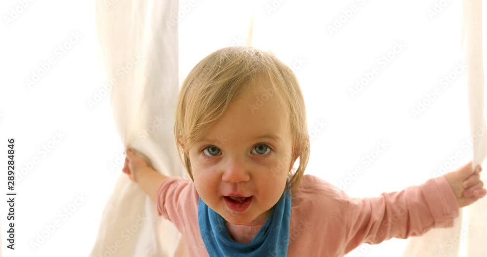 Cute little girl hiding behind a curtain, looking out and having fun ...