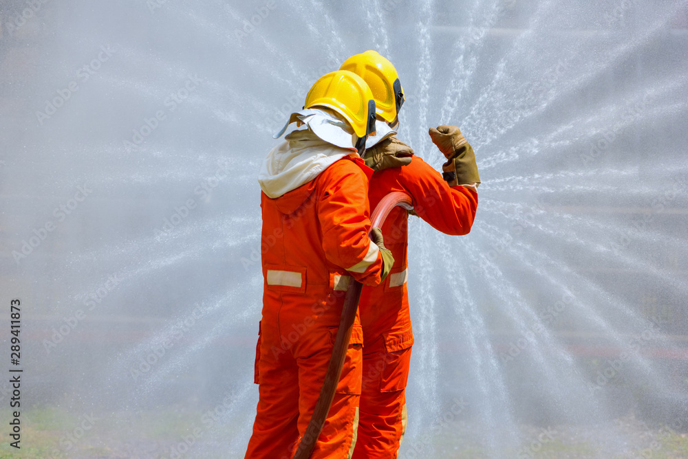 Two brave firefighter using extinguisher and water from hose for fire ...
