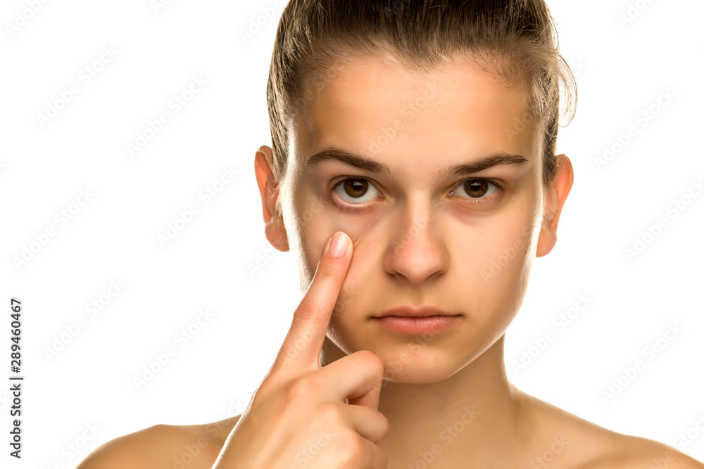 Young woman pulling her lower eyelid with her finger on white ...