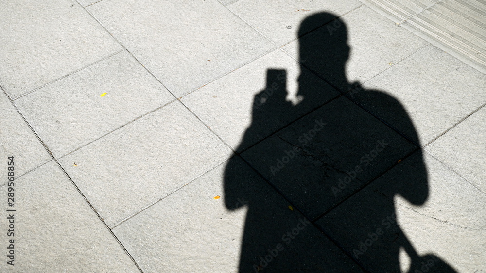 Shadow of a man looking at the screen of a smartphone, projected on a ...