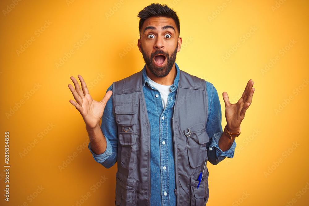 Handsome indian technician man wearing uniform over isolated yellow ...