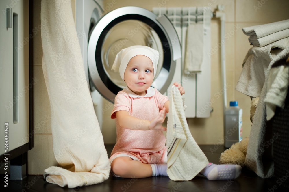 little blue-eyed girl sitting near the washing machine. Baby and ...