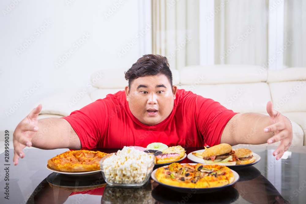 Overweight man hugging at a lot of unhealthy food Stock Photo | Adobe Stock