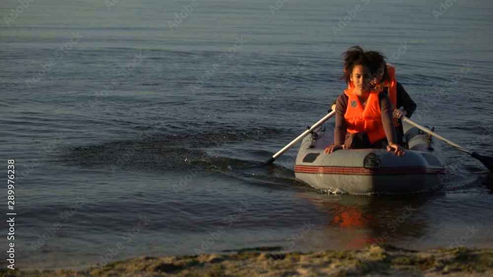 Women in life jackets rowing boat, falling at shore, terrified with ...