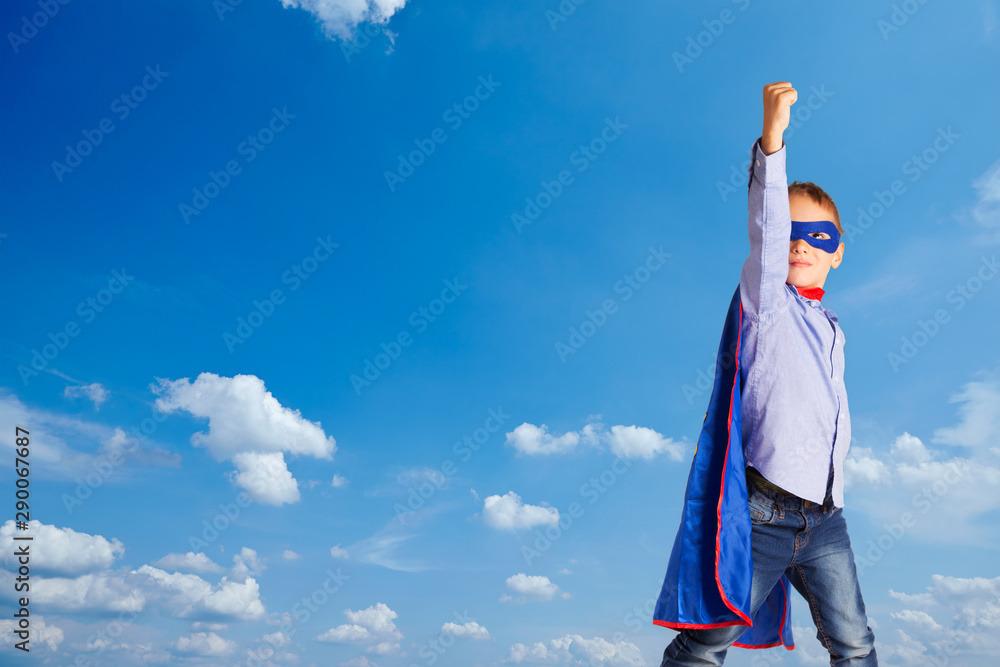 Young boy is playing like a superhero in front of a blue sky background ...
