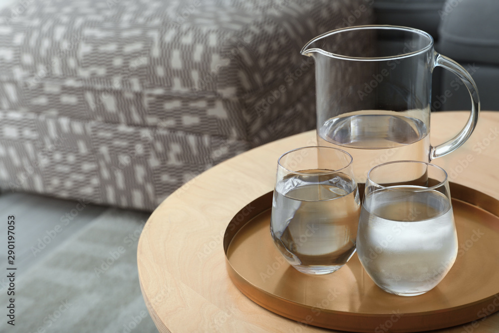 Tray with jug and glasses of water on wooden table in room, space for ...